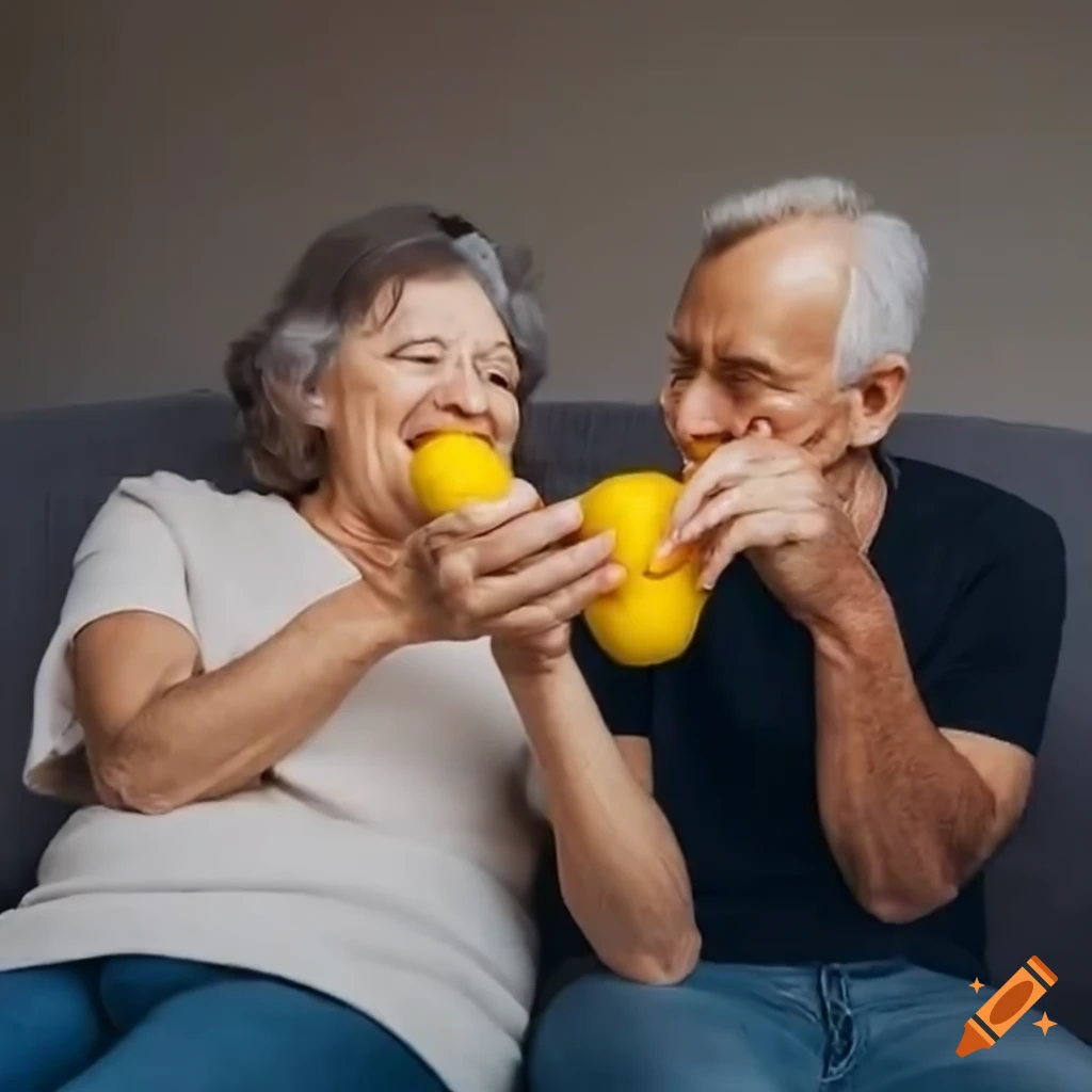 Smiling older couple sitting on a couch holding hands and biting into a ...